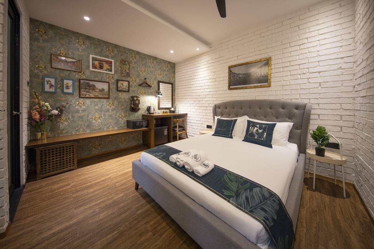 Quarto de hotel com uma cama grande, uma escrivaninha, uma cadeira e uma pequena mesa com uma planta.