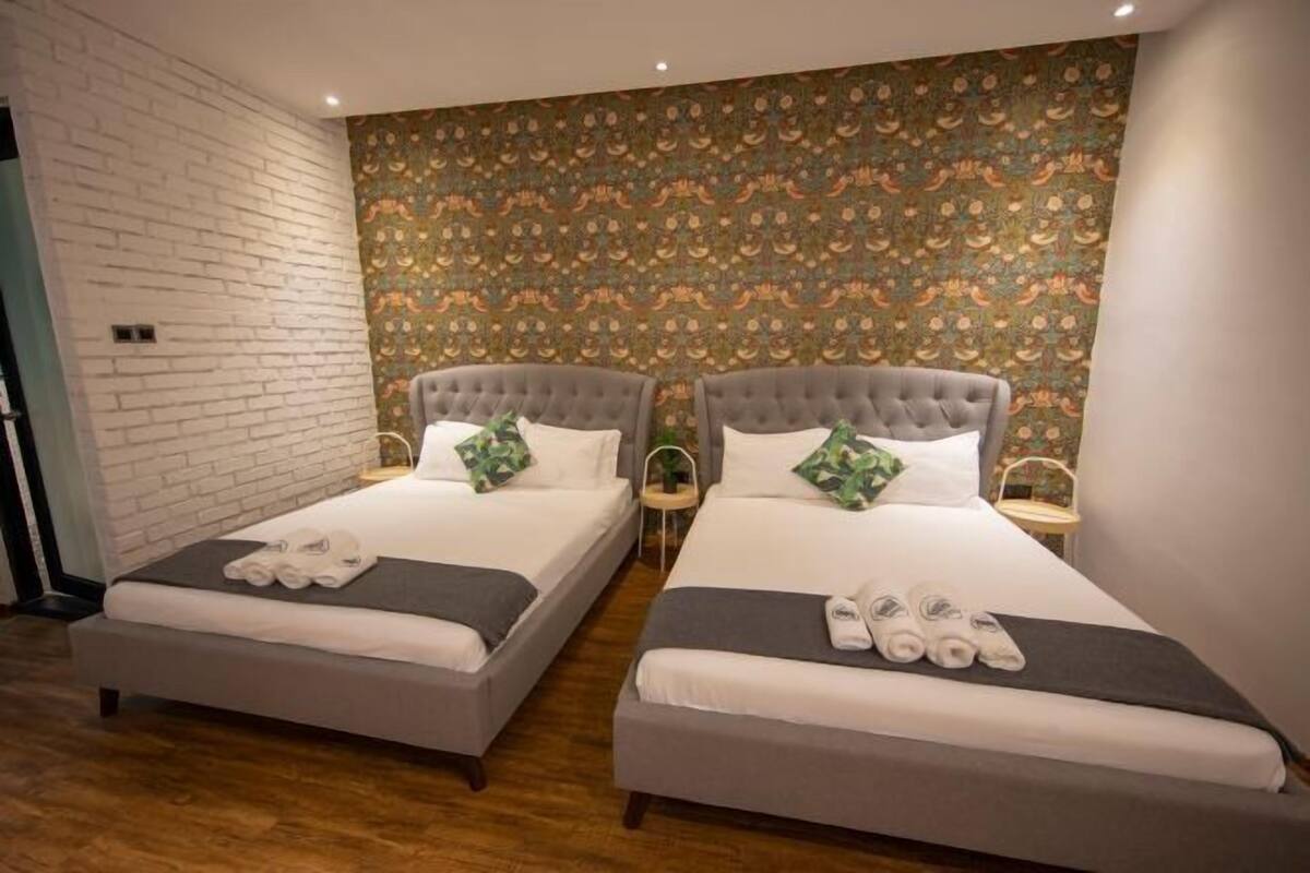 Quarto de hotel com duas camas, uma parede de tijolos e papel de parede estampado.