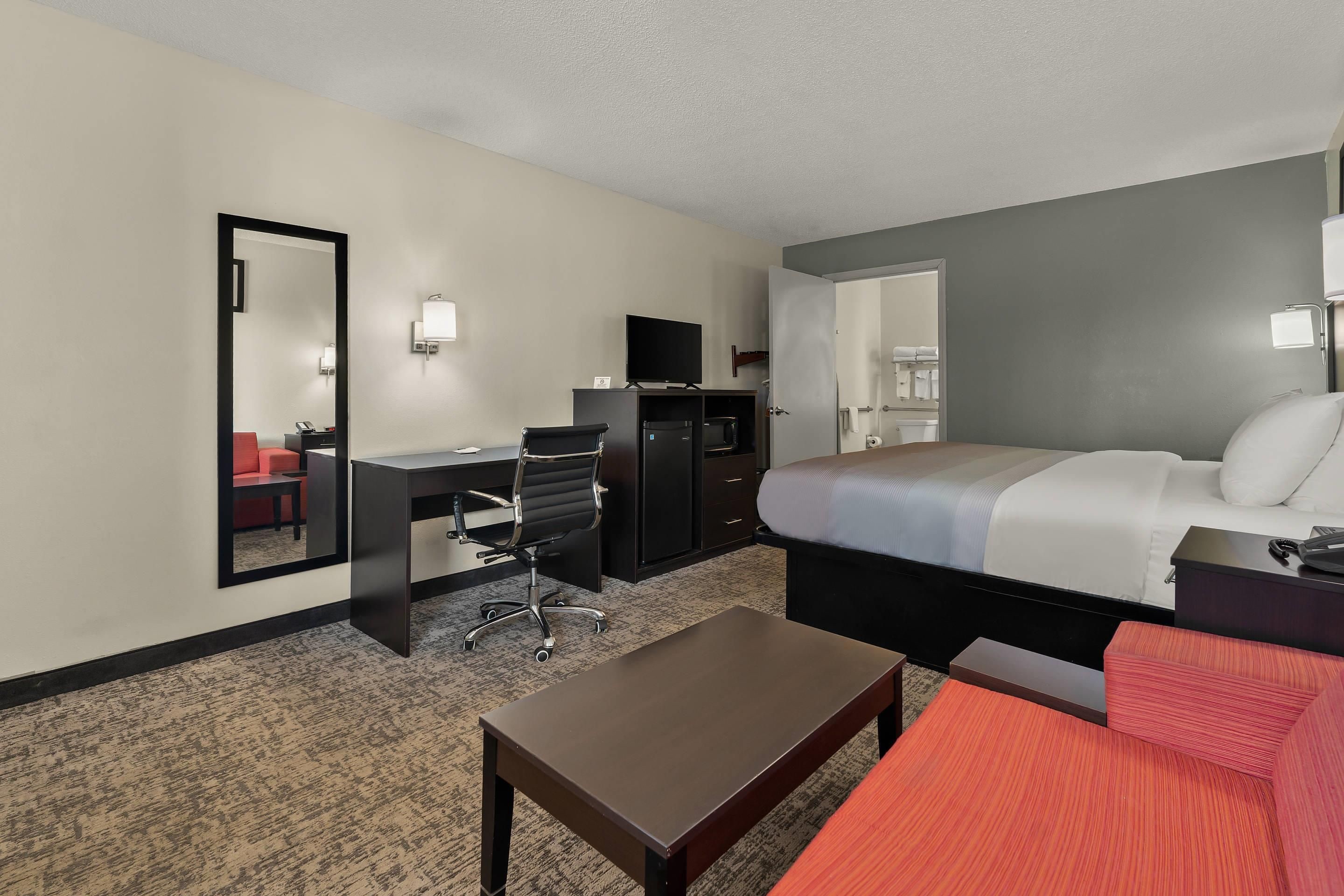 Quarto de hotel com cama, escrivaninha, cadeira e uma pequena mesa.