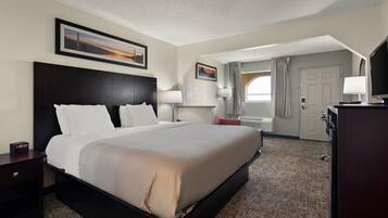 Quarto de hotel com cama grande, escrivaninha, cadeira, televisão e janela com cortinas.