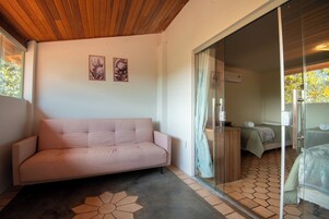 Quarto com sofá, cama e porta de vidro que dá para outro cômodo.