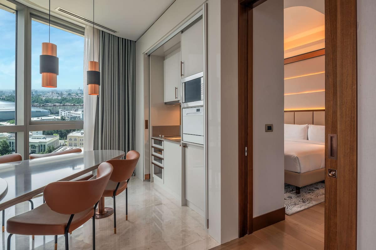Quarto de hotel moderno com área de refeições, cozinha compacta e uma cama.