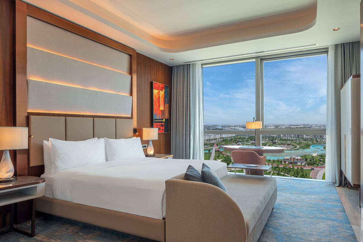 Quarto de hotel com uma cama grande, uma escrivaninha e vista para a paisagem urbana e um corpo d'água.