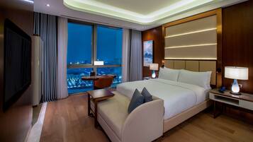 Quarto de hotel moderno com uma cama grande, uma escrivaninha e vista para a cidade à noite.