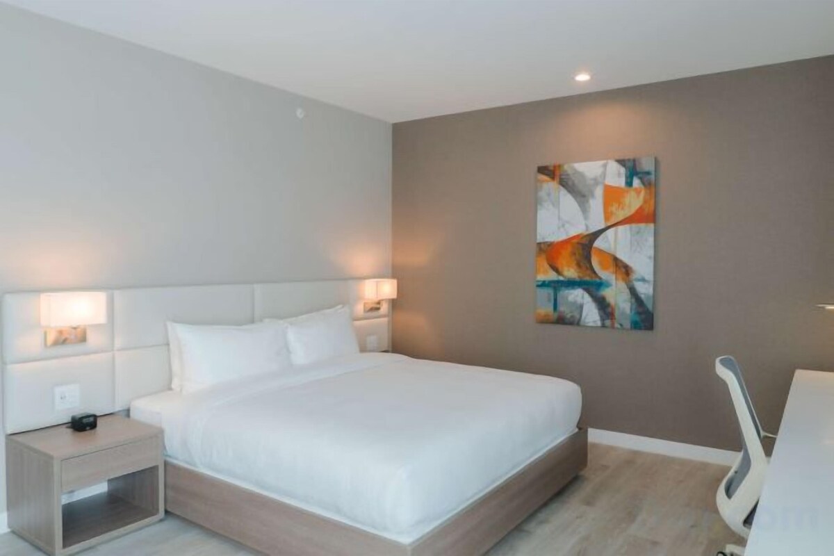Quarto de hotel com uma cama grande, luminárias de cabeceira, mesa de cabeceira e um quadro na parede.