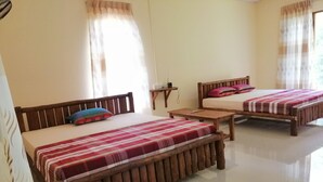 Quarto com duas camas de madeira, cada uma com colcha xadrez vermelha e branca e um travesseiro. Há uma pequena mesa de madeira entre as camas, e uma prateleira na parede com um abajur.