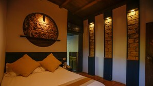 Quarto de hotel com uma cama grande, uma decoração circular na parede e detalhes em pedra nas paredes.