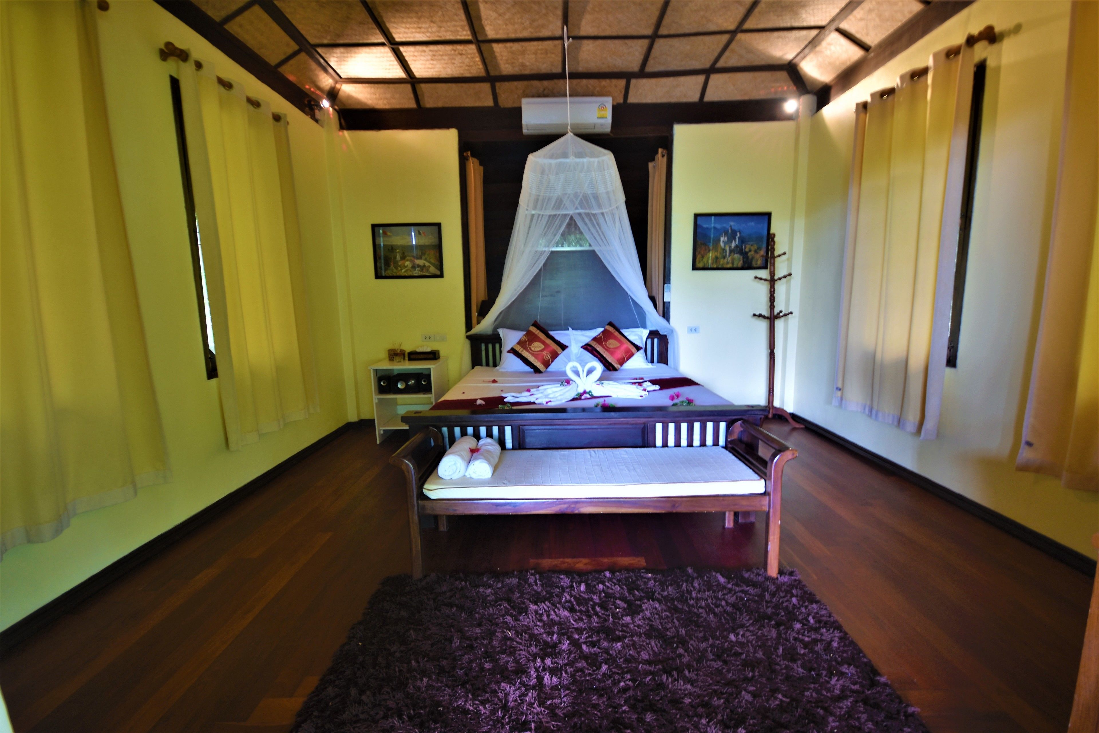 Quarto com cama, mesa de cabeceira, chão de madeira e tapete.