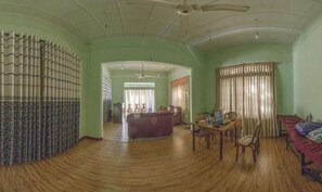 Quarto com piso de madeira, sofá, escrivaninha com computador e uma cadeira.