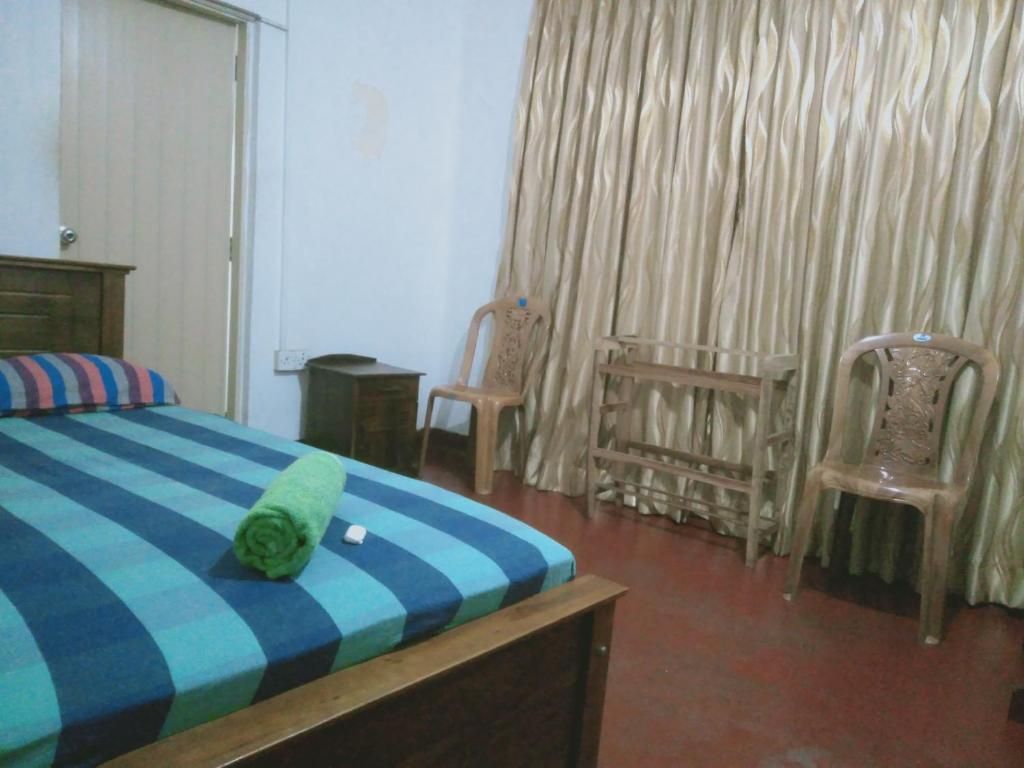 Quarto com cama, cabeceira de madeira, mesa pequena, duas cadeiras e cortina.
