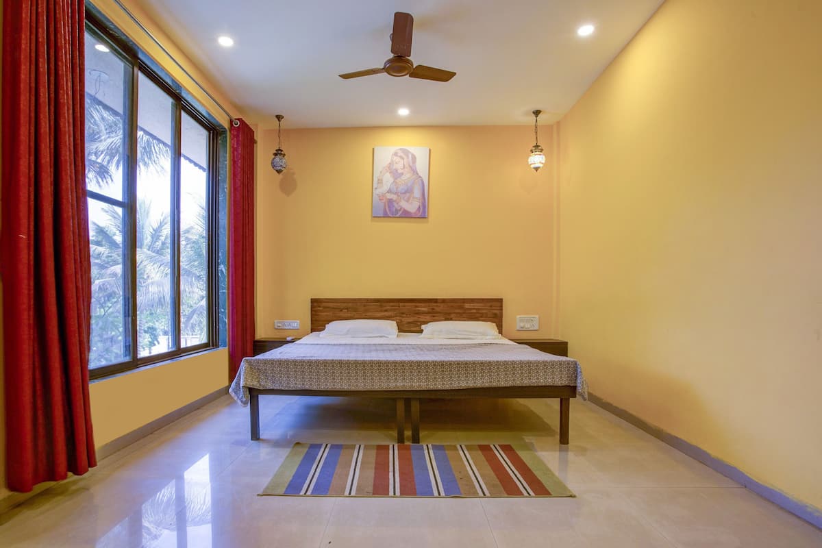 Quarto com cama, ventoinha no teto, janela com cortinas e um quadro na parede.