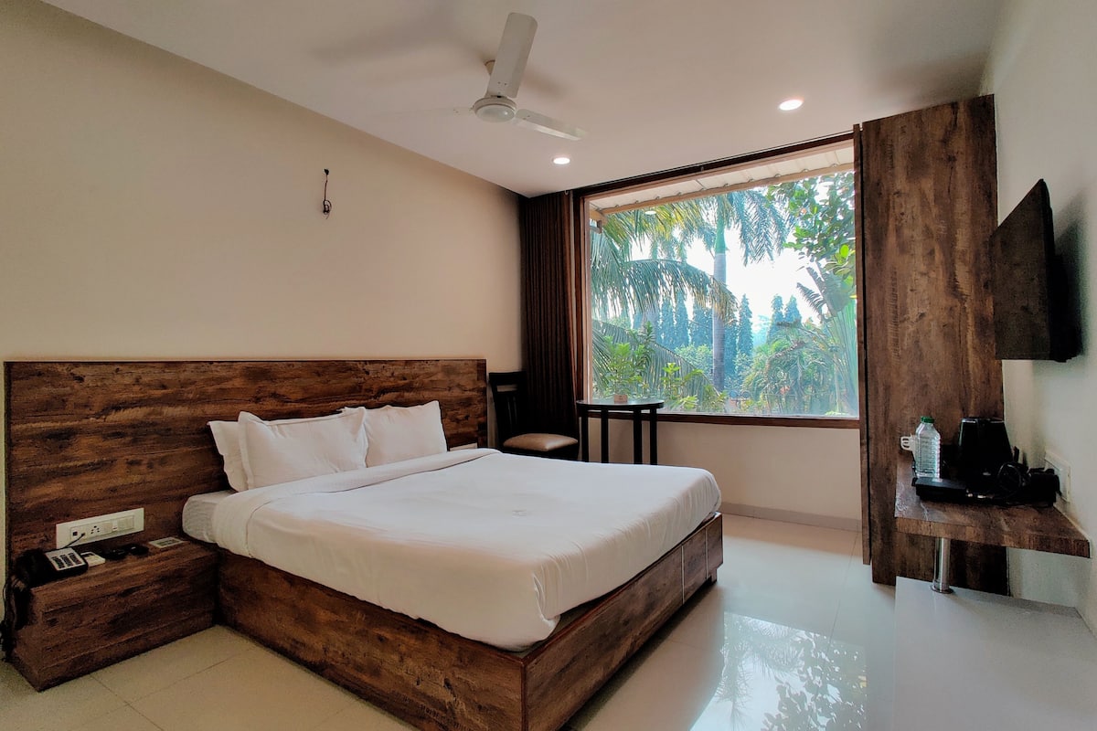 Quarto moderno com cabeceira de madeira, uma cama grande, uma mesinha, uma cadeira e uma TV fixada na parede.
