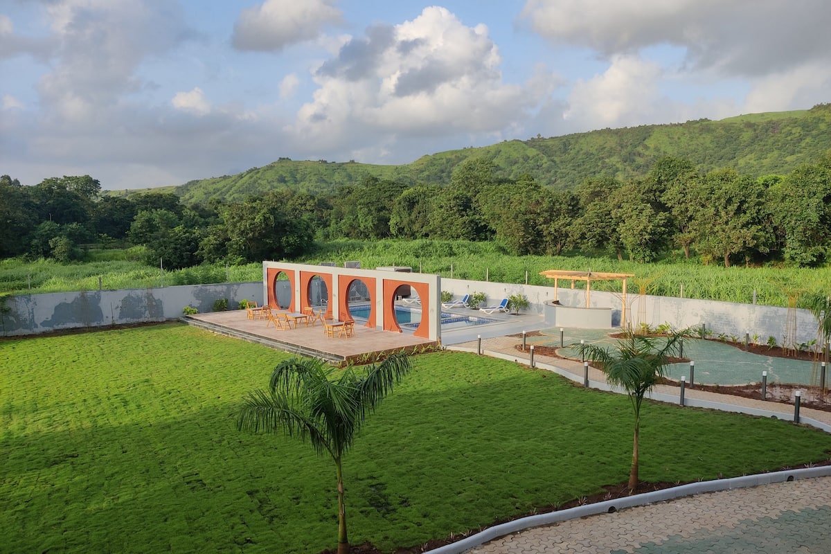 Uma área de piscina com espreguiçadeiras e um pérgola, cercada por vegetação exuberante e colinas.