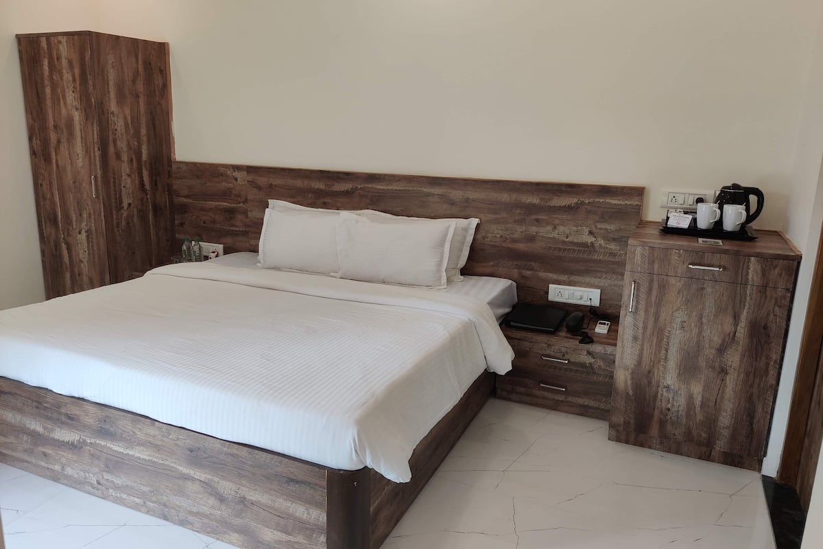 Quarto com cabeceira de madeira, cama com roupa de cama branca, mesa de cabeceira com cafeteira e guarda-roupa de madeira.