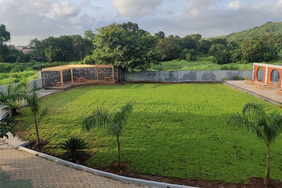 Uma área externa gramada com um espaço coberto para sentar e um muro com aberturas circulares.