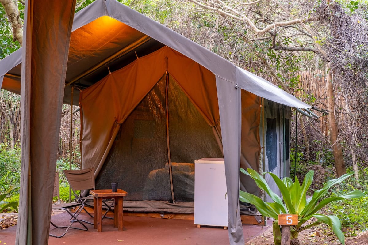Acomodação em tenda com cama, mesa e geladeira.