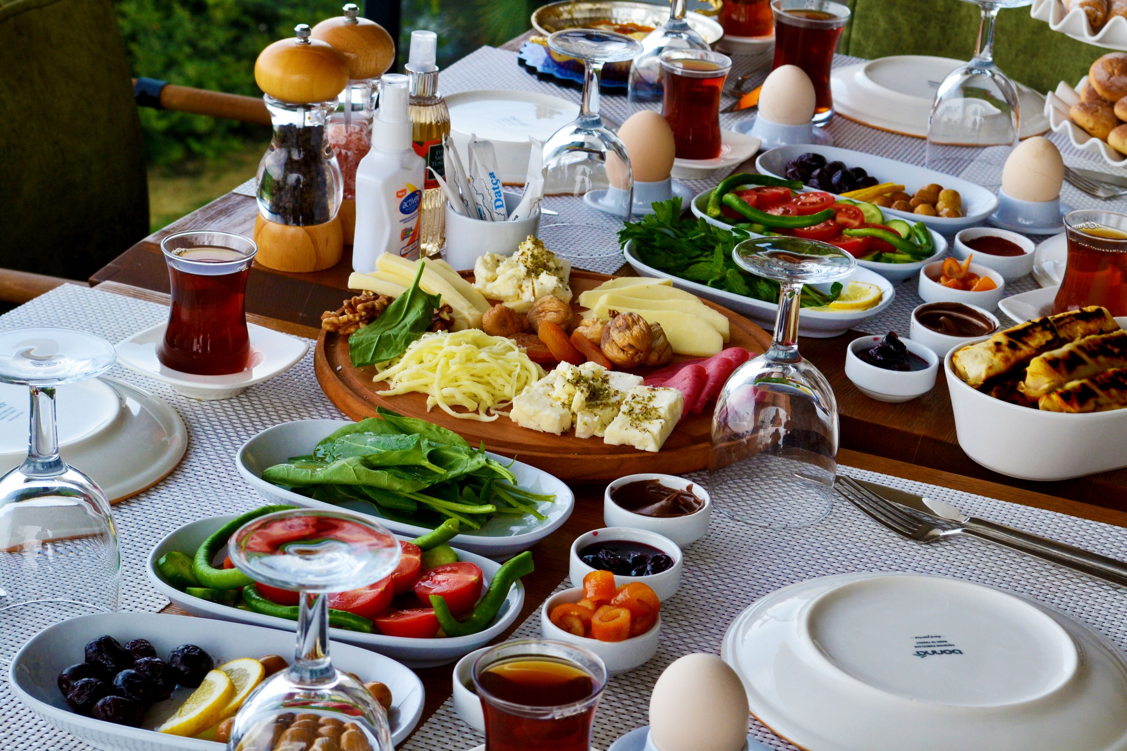 Uma mesa posta para refeição com diversos pratos, incluindo saladas, carnes e pão, além de copos de chá e acompanhamentos.