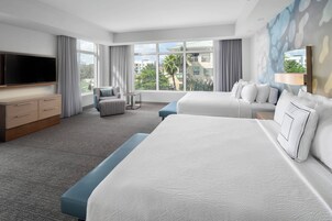 Quarto de hotel com duas camas, uma TV de tela plana, uma escrivaninha e vista para a cidade.