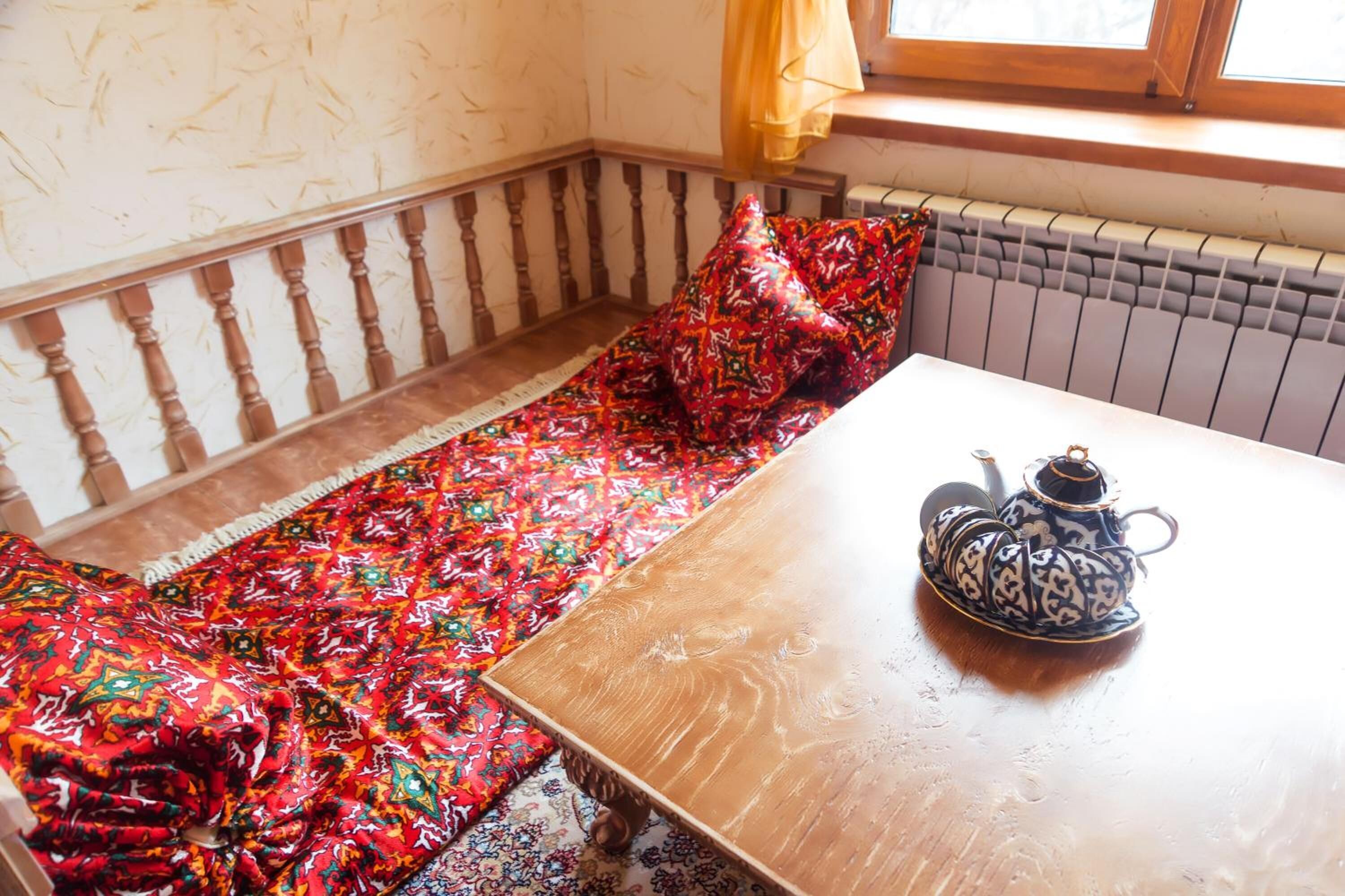 Quarto com um banco de madeira, um tapete estampado e uma mesa com uma chaleira.