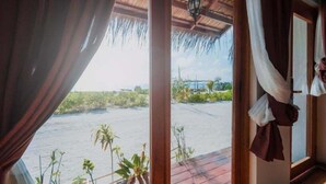 Quarto com uma grande janela com vista para um corpo de água, um deck de madeira e vegetação, além de uma ponte ao longe.