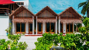 Um resort com estruturas de telhado de palha, janelas amplas e um edifício branco ao fundo.