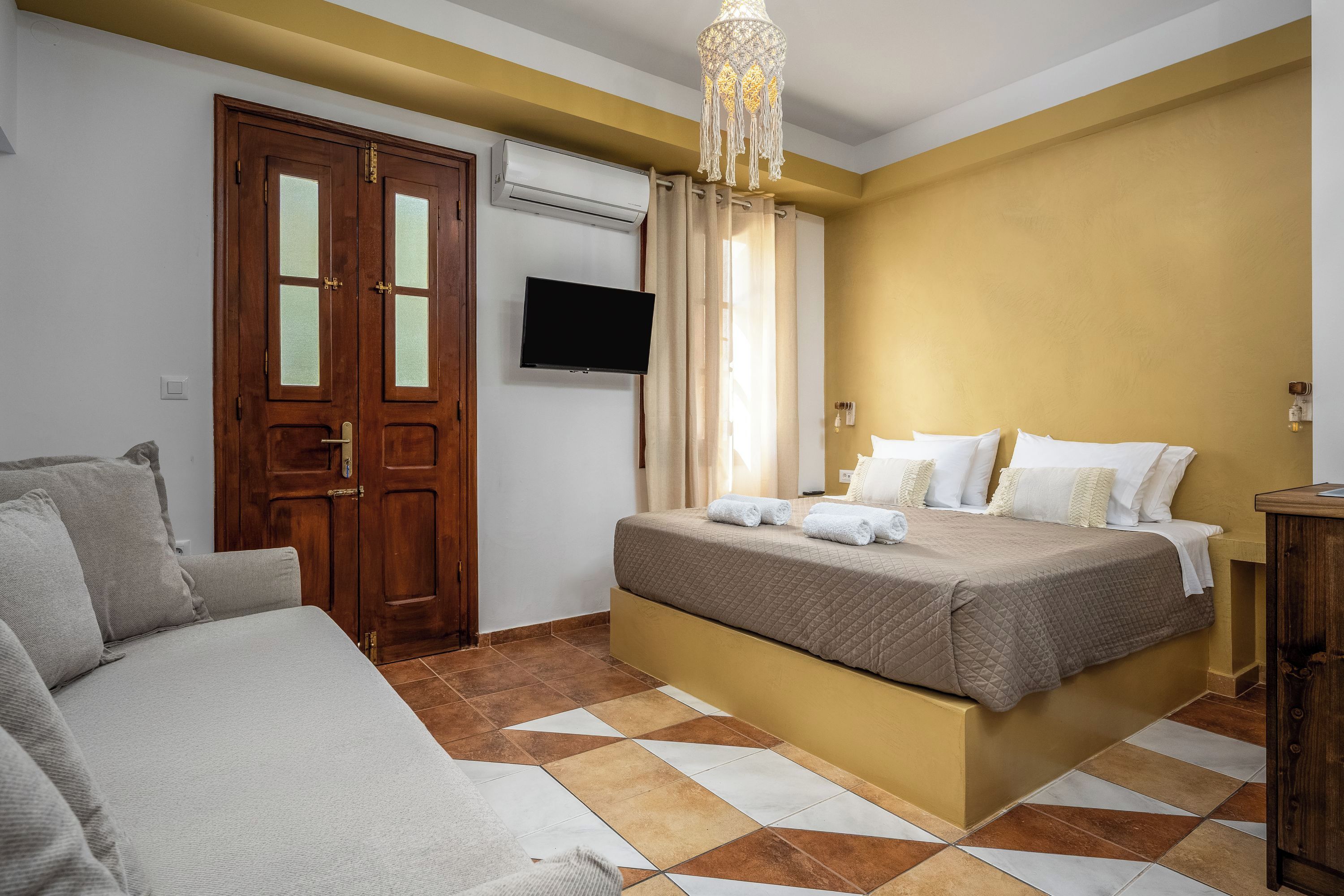 Quarto com cama, sofá, televisão e lustre.