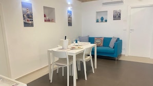 Uma sala de jantar com uma mesa e cadeiras, um sofá azul e uma porta.