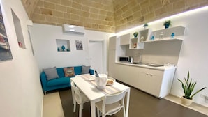 Um espaço de estar compacto com área de refeições, cozinha compacta e um sofá azul com almofadas estampadas.