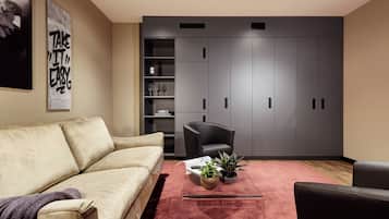 Uma sala de estar moderna com um sofá bege, uma poltrona preta e um tapete vermelho. Há uma estante com objetos decorativos e um guarda-roupa cinza grande.