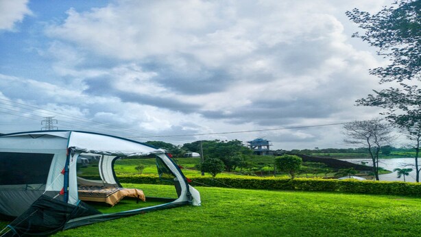 Uma tenda montada numa área gramada, com vista para um lago e árvores ao fundo.