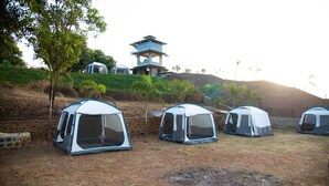 Um camping com várias tendas e uma torre de vigia ao fundo.