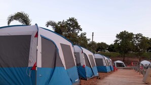 Fileira de tendas azuis e cinzentas sobre um terreno de terra, dispostas num camping.