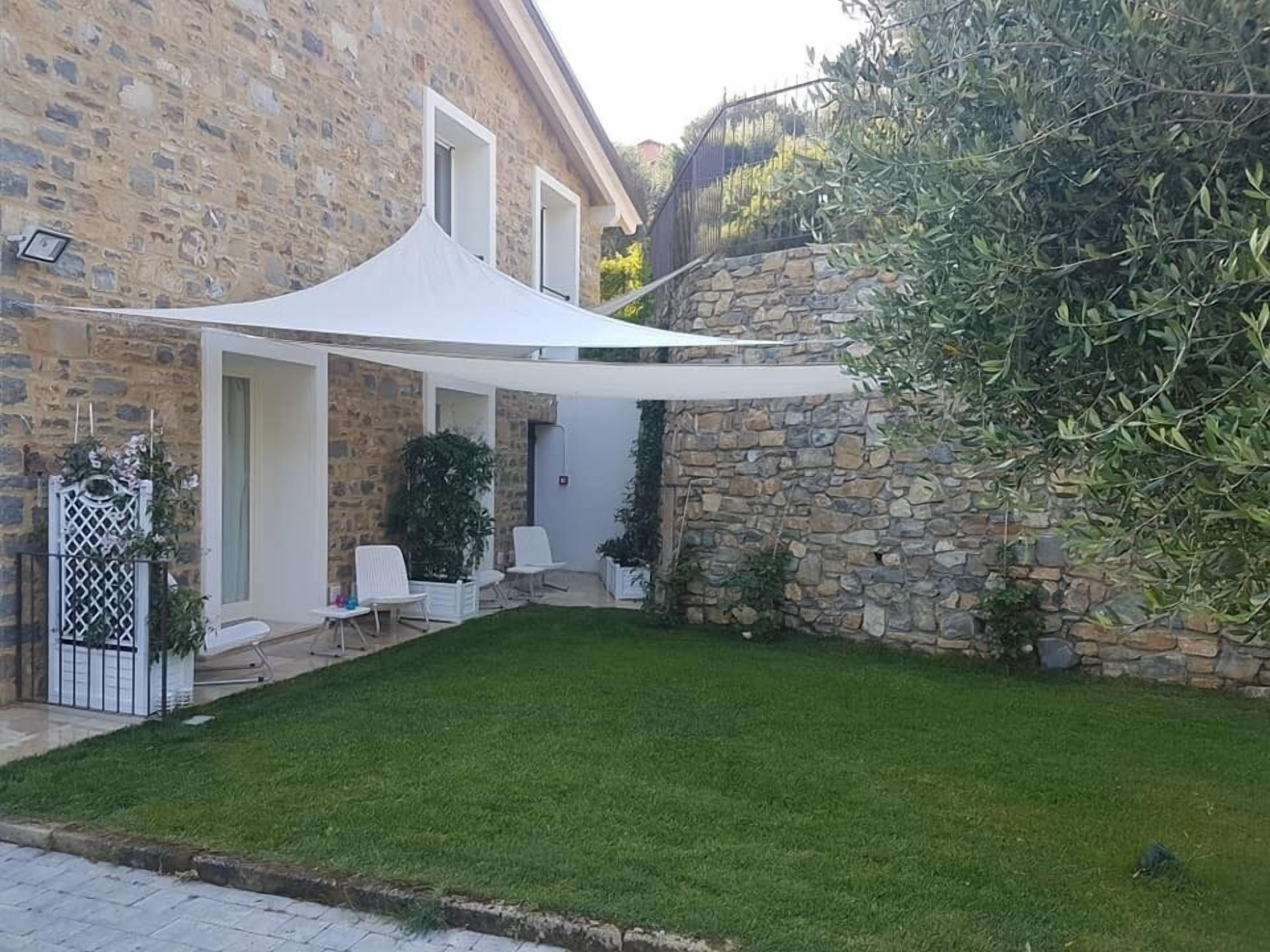 Um edifício de pedra com toldo branco sobre um pátio com cadeiras brancas e uma pequena mesa.