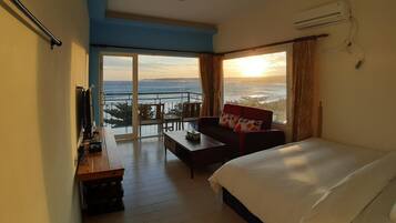 Quarto de hotel com cama, escrivaninha, cadeira e varanda com vista para o mar.