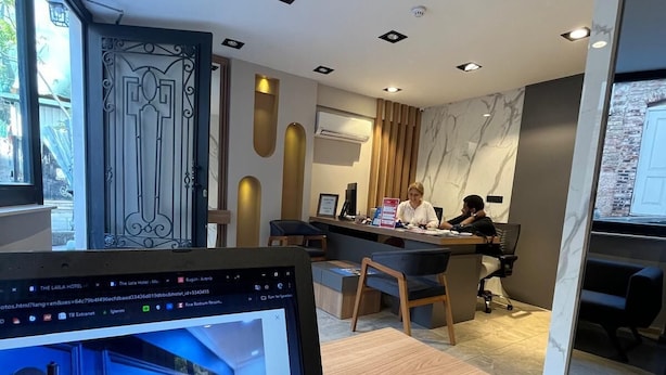 Quarto de hotel moderno com escrivaninha de madeira, um laptop exibindo uma galeria de fotos, uma janela grande e uma porta decorativa.
