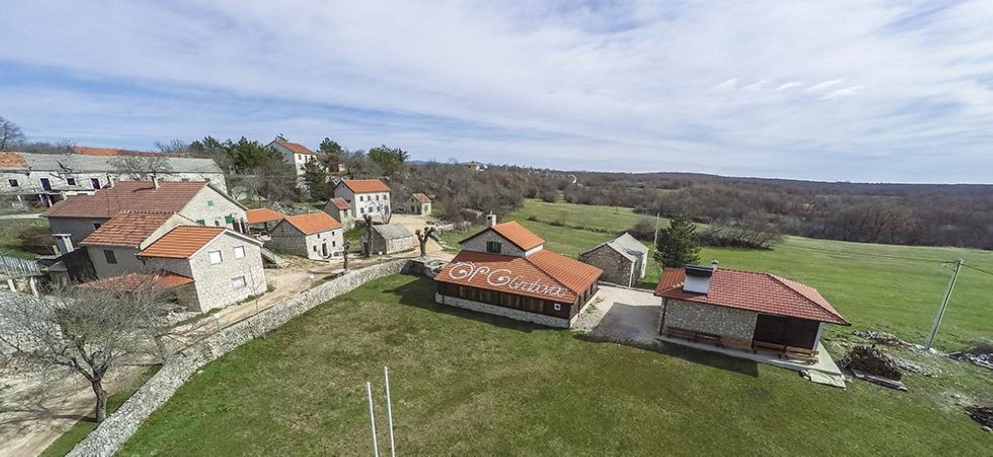 Uma propriedade rural com vários edifícios, incluindo uma casa principal com telhado vermelho e um celeiro.