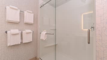 Um banheiro moderno com box de vidro, várias toalhas brancas em um porta-toalhas e um padrão geométrico de azulejos nas paredes.