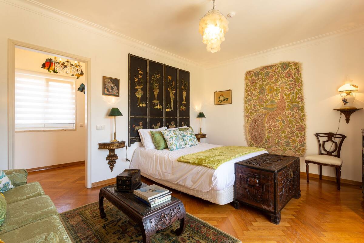 Quarto com cama, mesas de cabeceira, uma cadeira, abajur e um biombo decorativo.