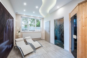 Uma sala de spa moderna com uma grande janela, uma cascata na parede e duas poltronas reclináveis.