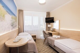 Quarto de hotel com cama, escrivaninha, cadeira, televisão e janela com cortinas.