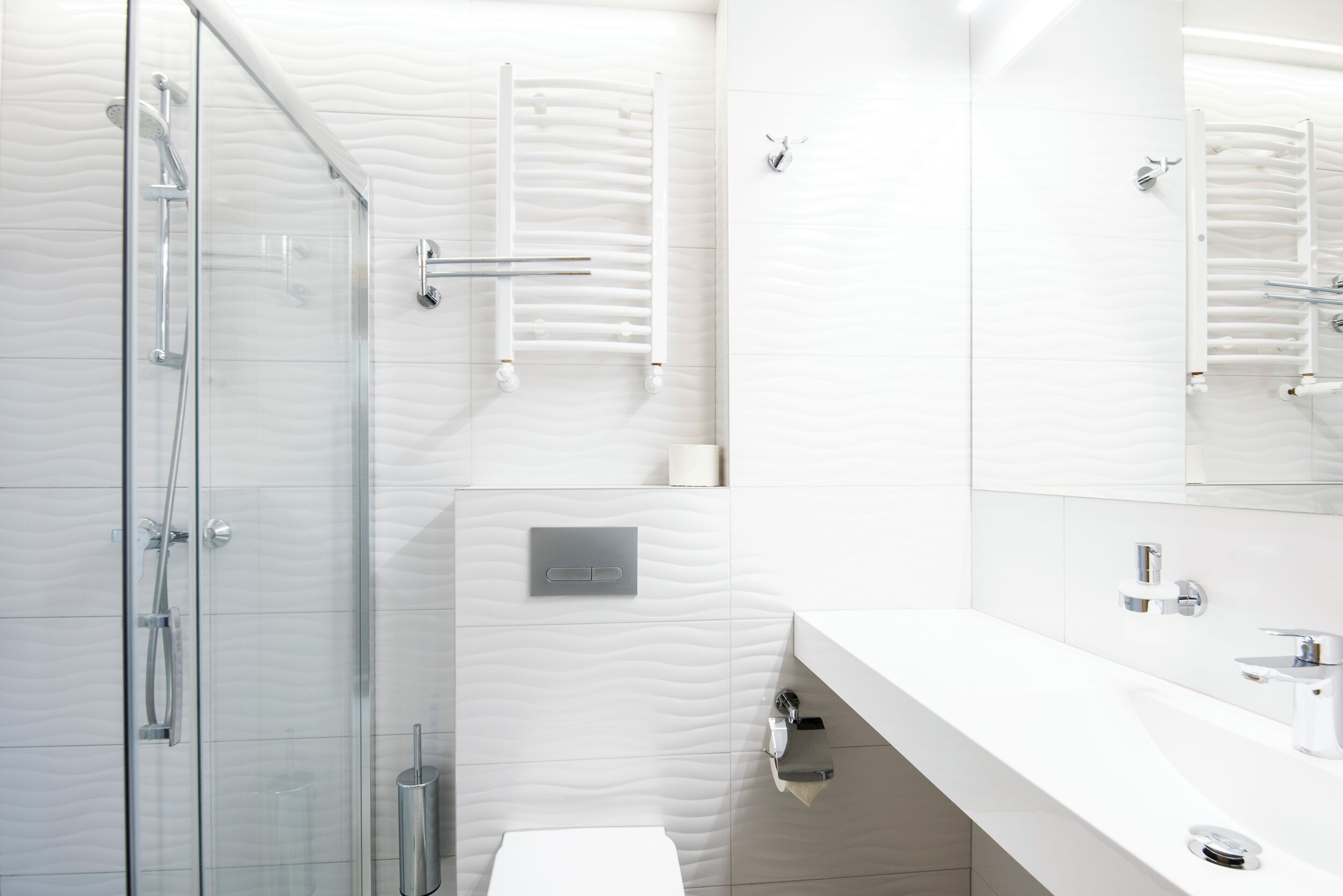 Um banheiro moderno com box de vidro, um espelho sobre o balcão branco e um porta-toalhas.