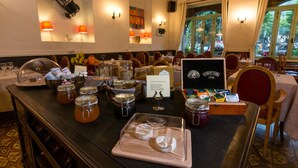 Disposição de buffet com diversos alimentos e acompanhamentos, incluindo potes de conservas e uma bandeja de doces.