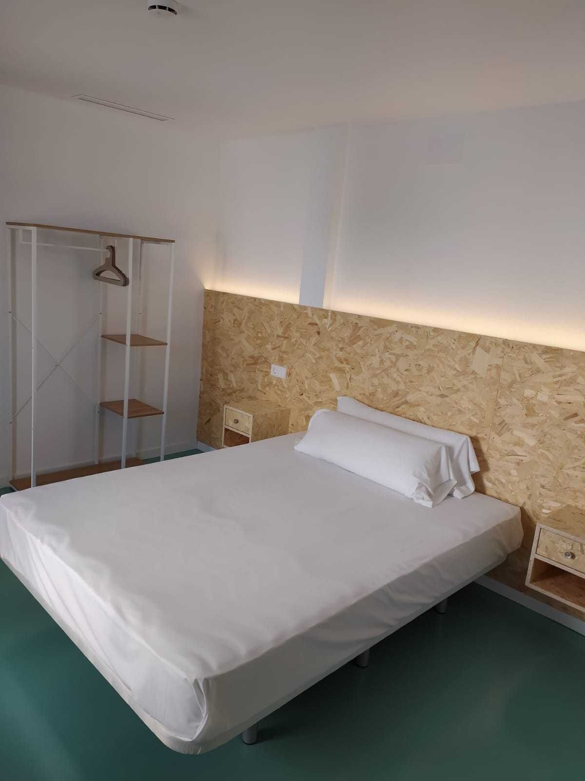 Uma cama bem arrumada num quarto com cabeceira de madeira, um guarda-roupa de madeira e uma pequena mesa de cabeceira.