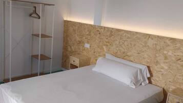 Uma cama bem arrumada num quarto com cabeceira de madeira, um guarda-roupa de madeira e uma pequena mesa de cabeceira.
