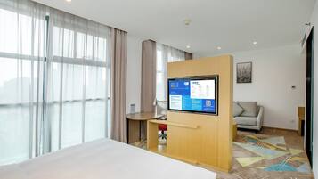 Quarto de hotel com cama, escrivaninha, televisão e sofá.