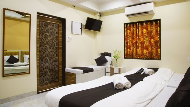 Quarto de hotel com duas camas, uma escrivaninha, uma cadeira, TV fixada na parede e ar condicionado.