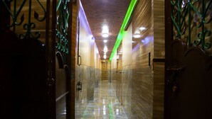 Corredor com piso de mármore espelhado, grades decorativas verdes e teto com iluminação embutida.