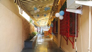 Um corredor estreito com chão de azulejos, toldo listrado e persianas vermelhas.
