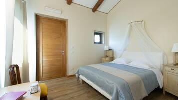 Um quarto com cama, mesas de cabeceira, uma porta de madeira, uma janela pequena e uma cadeira.