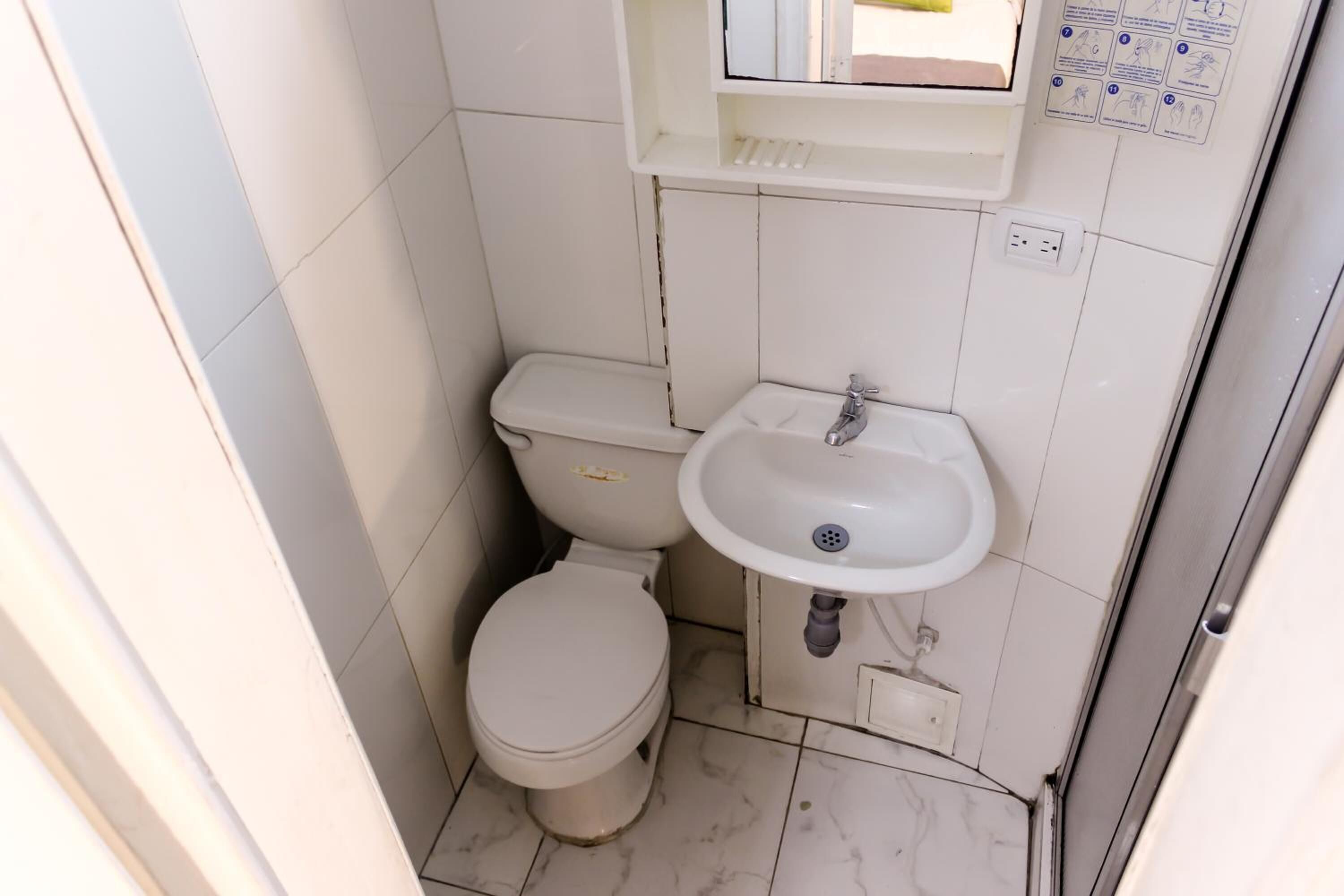 Casa de banho pequena e compacta com sanita, lavatório e espelho sobre o lavatório.
